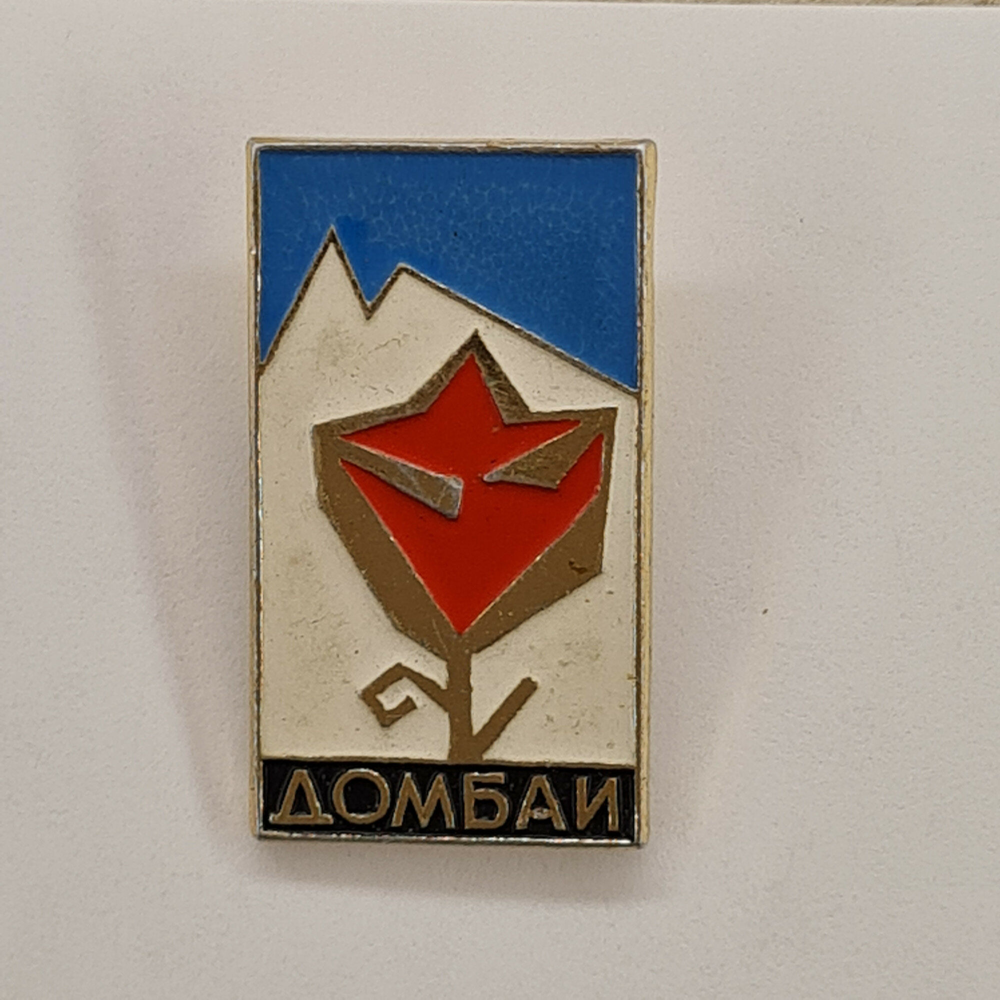 Домбай. Красный треугольный символ на фоне гор. Винтажный значок.