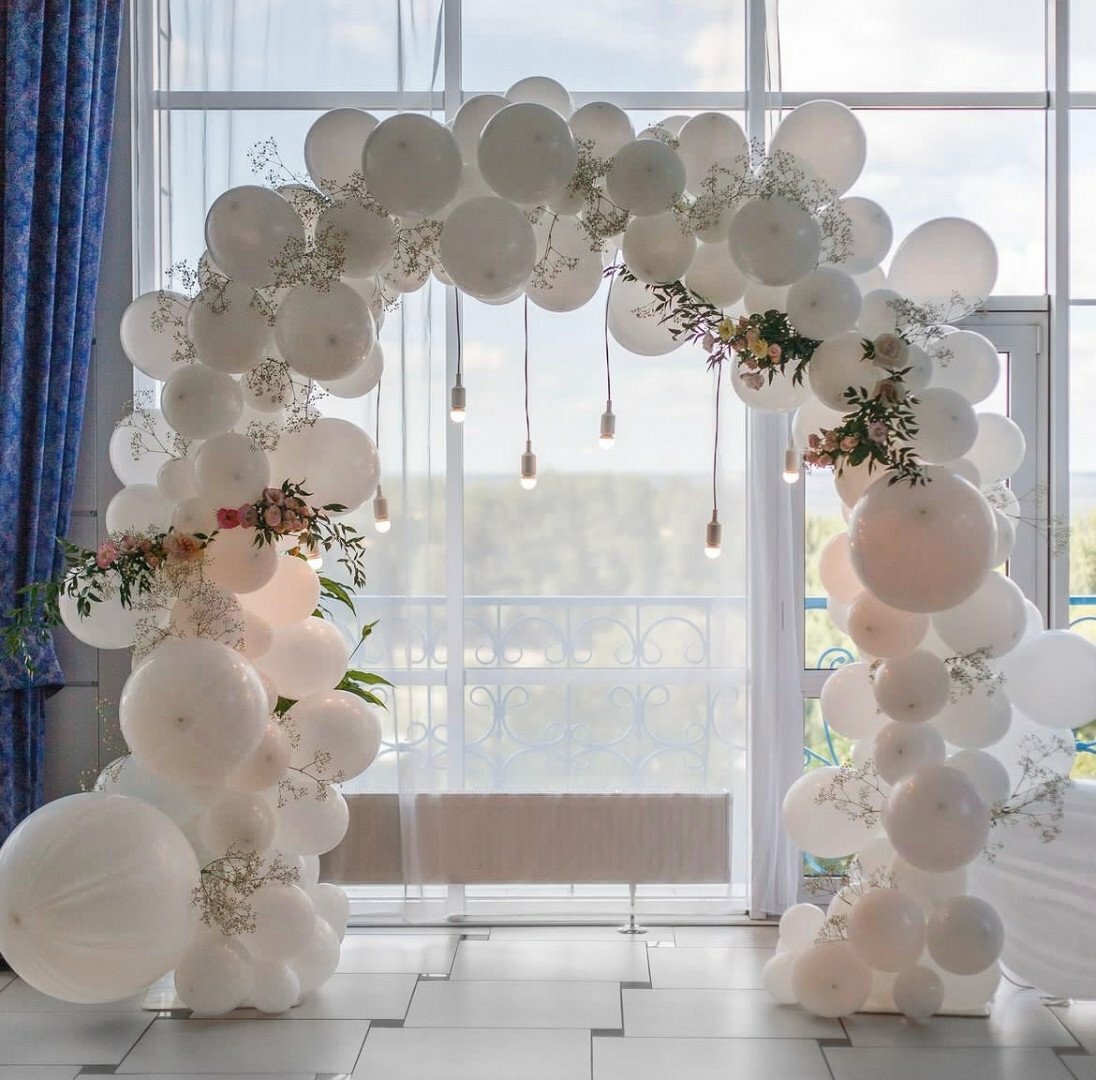 Белая арка из шаров разного размера с искусственными цветами
