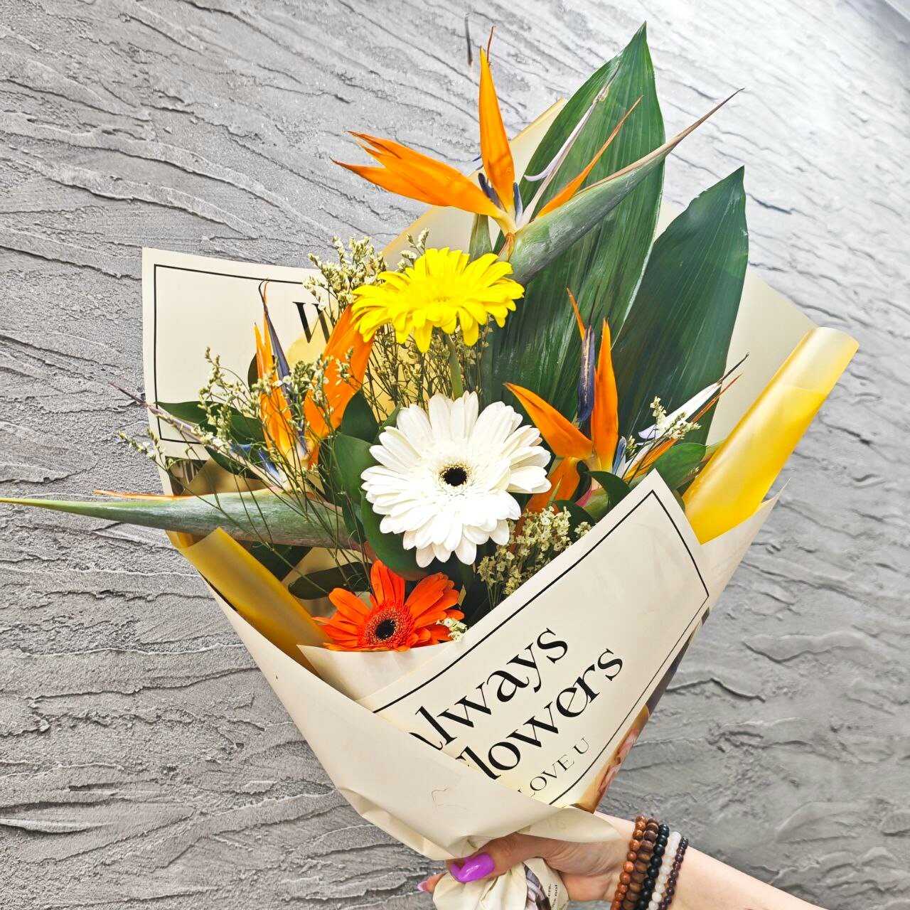 Экзотический букет из цветов стрелиция, гербера, лимониум с зеленью аспидистра и рускус