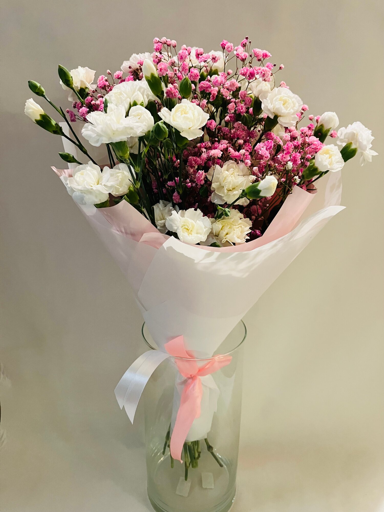Букет из 11 белых, свежих, кустовых гвоздик с розовой гипсофилой, в дизайнерской упаковке, атласный бант.
