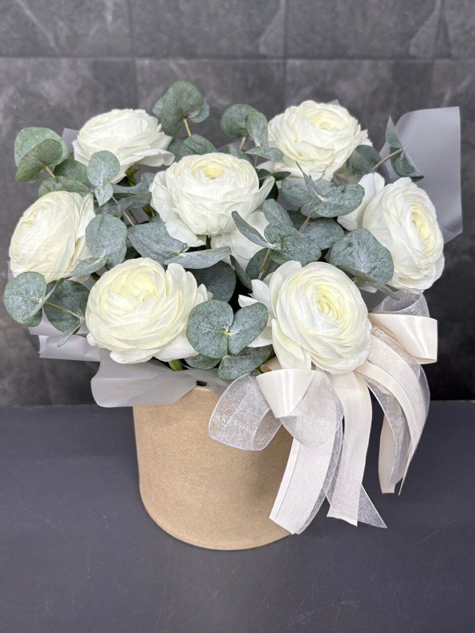 Композиция из сезонных ранункулюсов в шляпной коробке ароматным эвкалиптом размер S