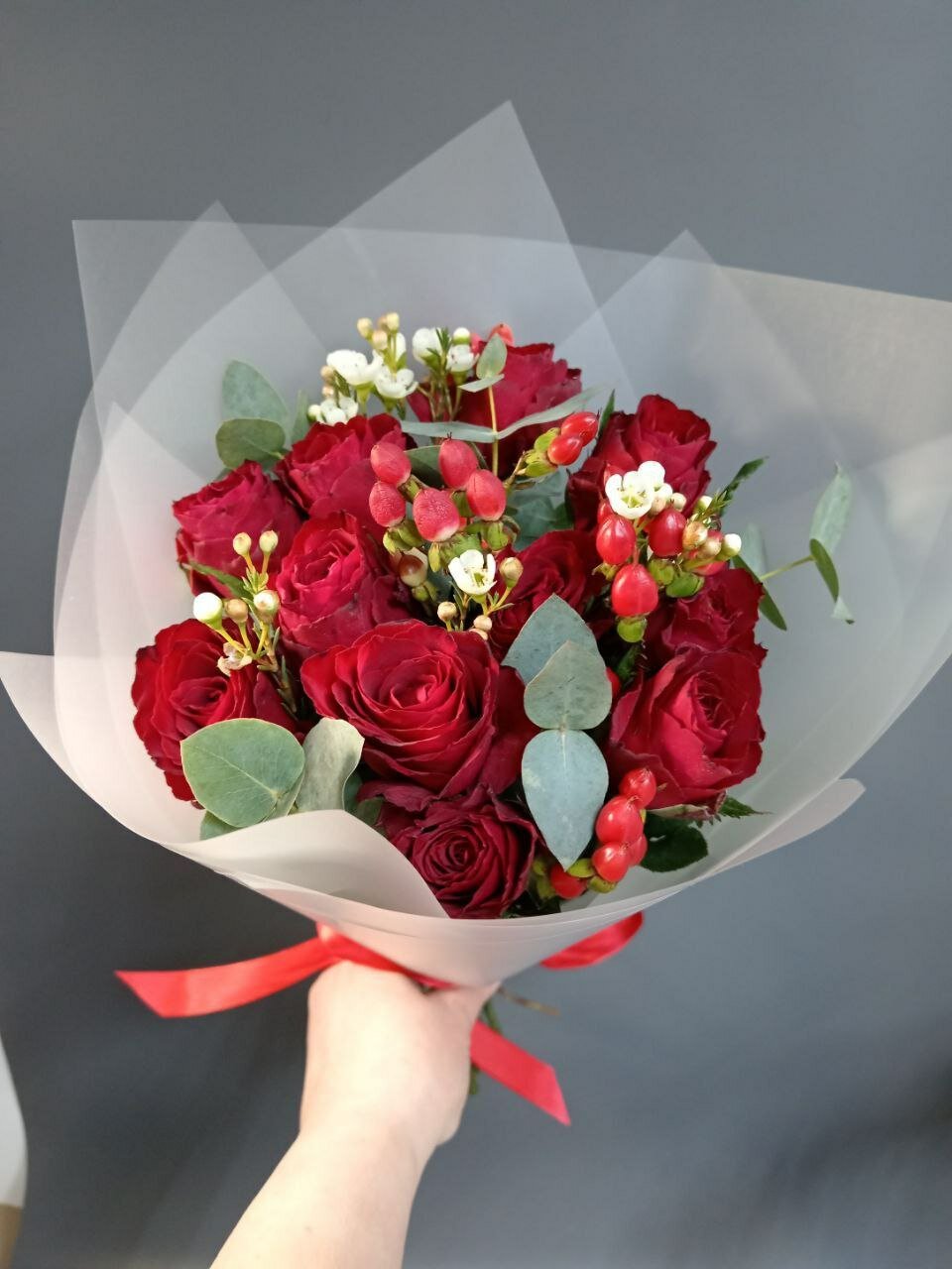 Букет из красной розы с красными ягодами гиперикума, хамилациум и эвкалипт.