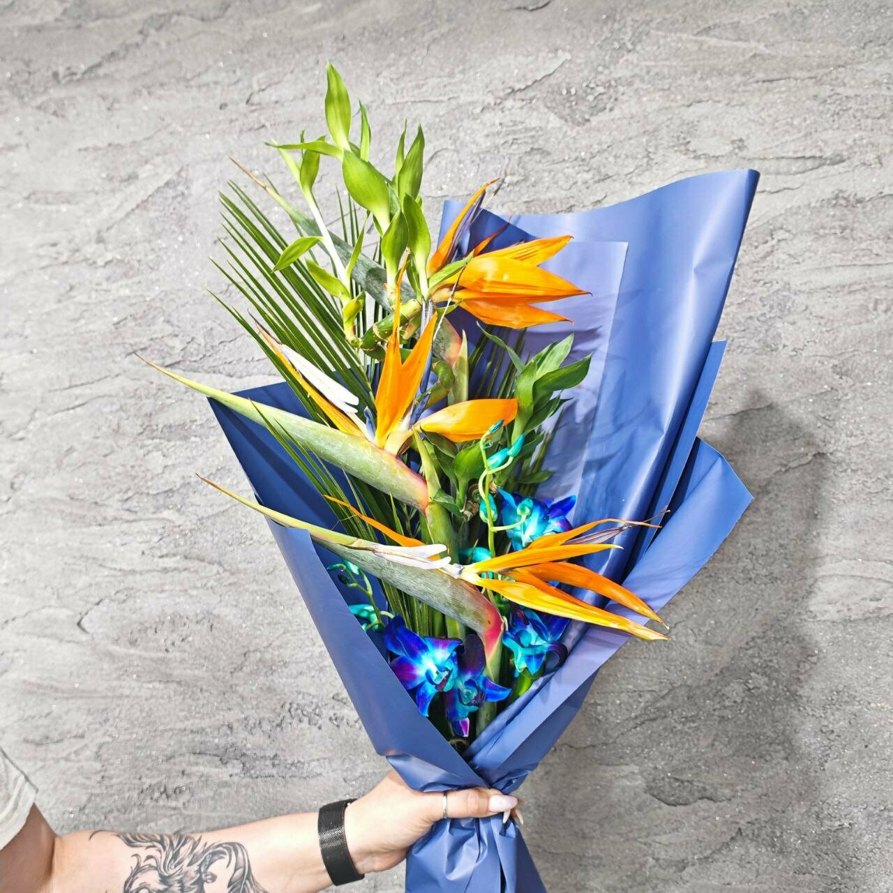 Экзотический букет из стрелиции, синих орхидей дендробиум, бамбука лаки с зеленью робелини