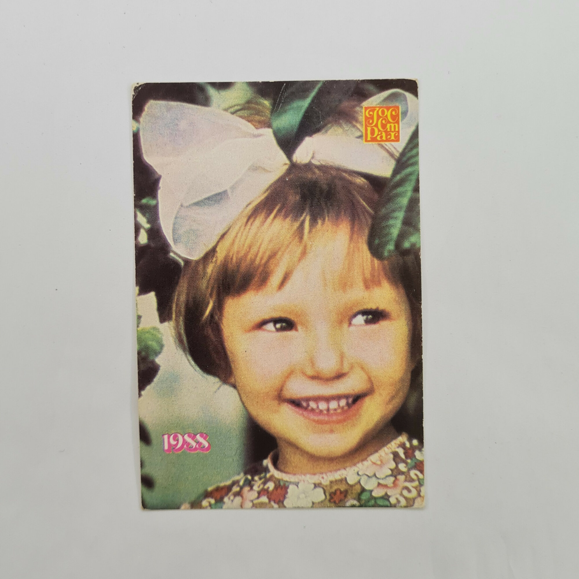 Карманный календарик 1988. Улыбающаяся девочка с бантом на фоне зелени. Календарь винтажный