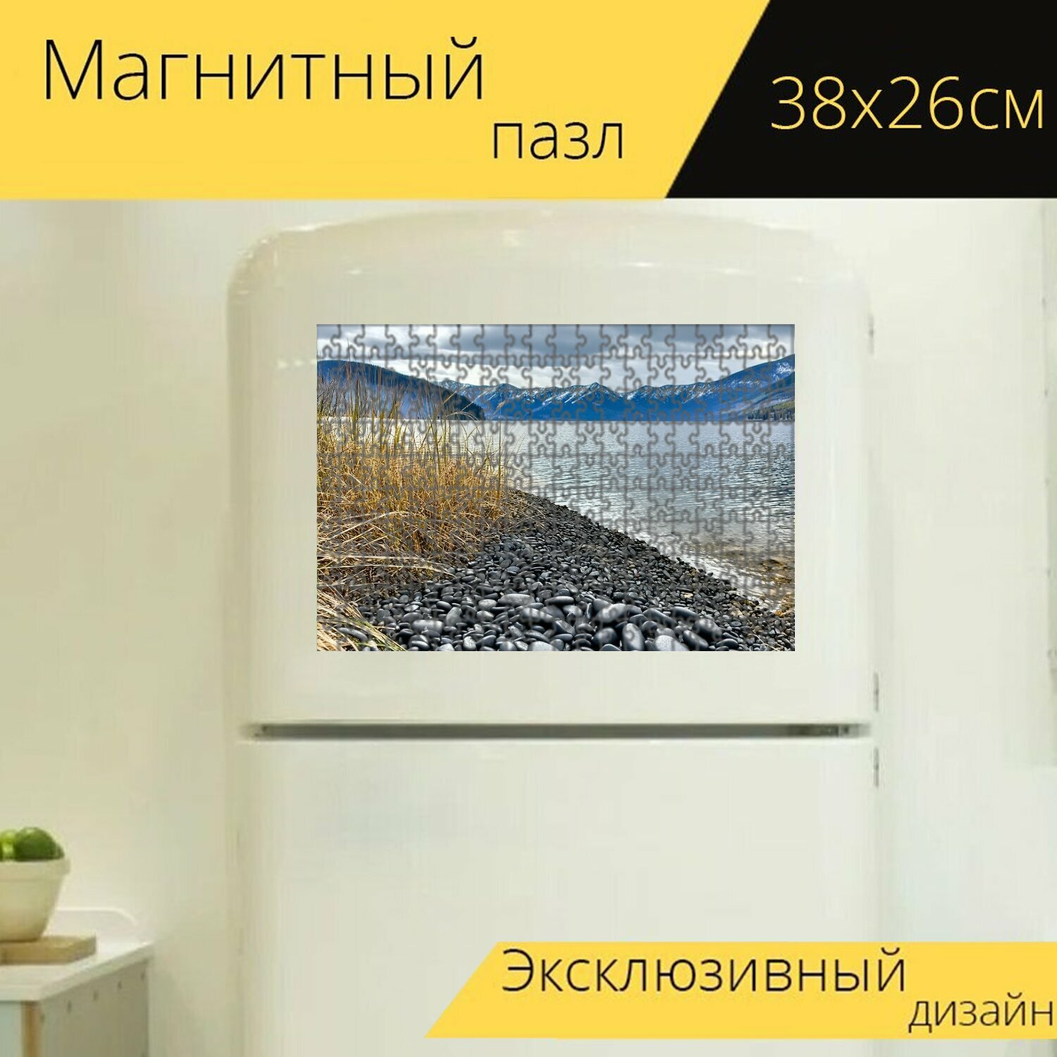 Магнитный пазл "Темная галька на берегу озера, окруженная сухими травами, ведущая к спокойной воде, вдалеке величественные горы под облачным небом." для интерьера, 38х26 см.