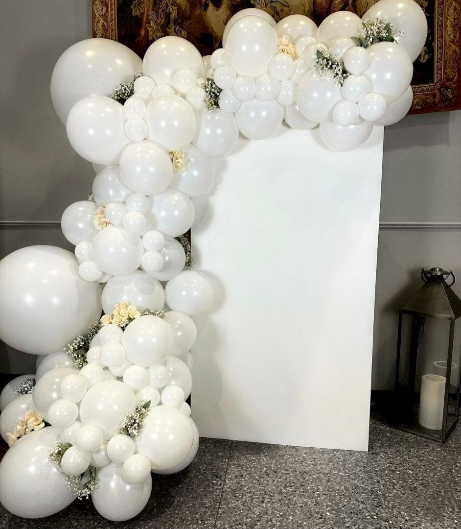 Белая фотозона из латексных шаров с декоративными цветами и баннером