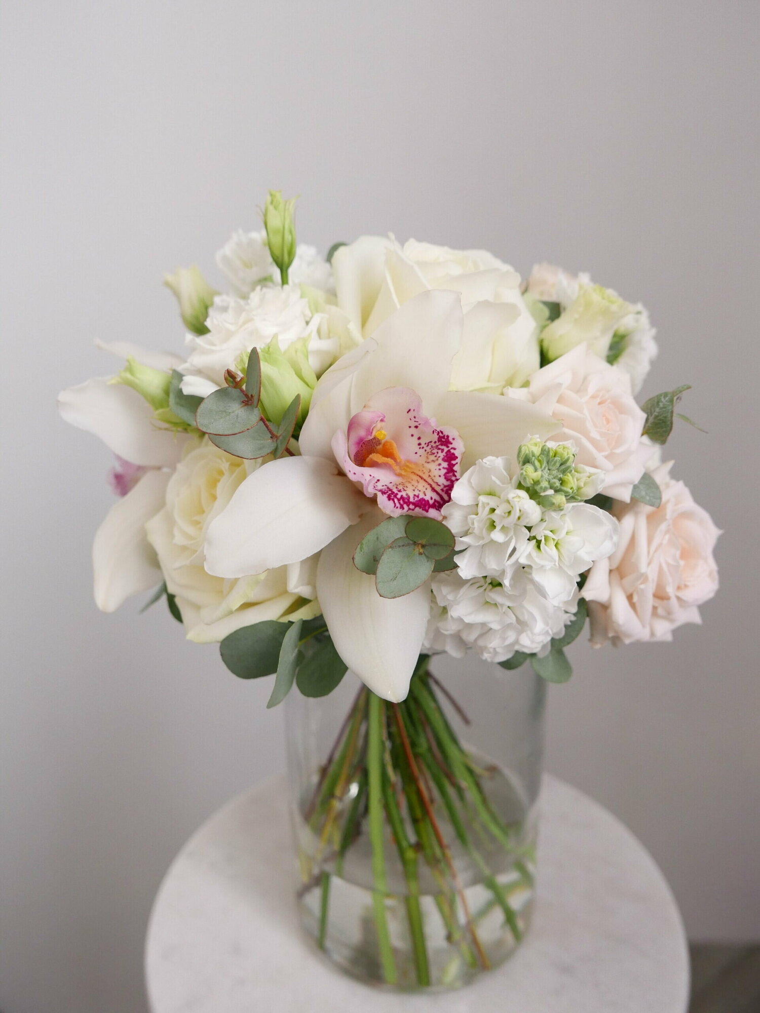 Небольшой белый букет с розами и орхидеями в вазе от студии цветов клумба. москва